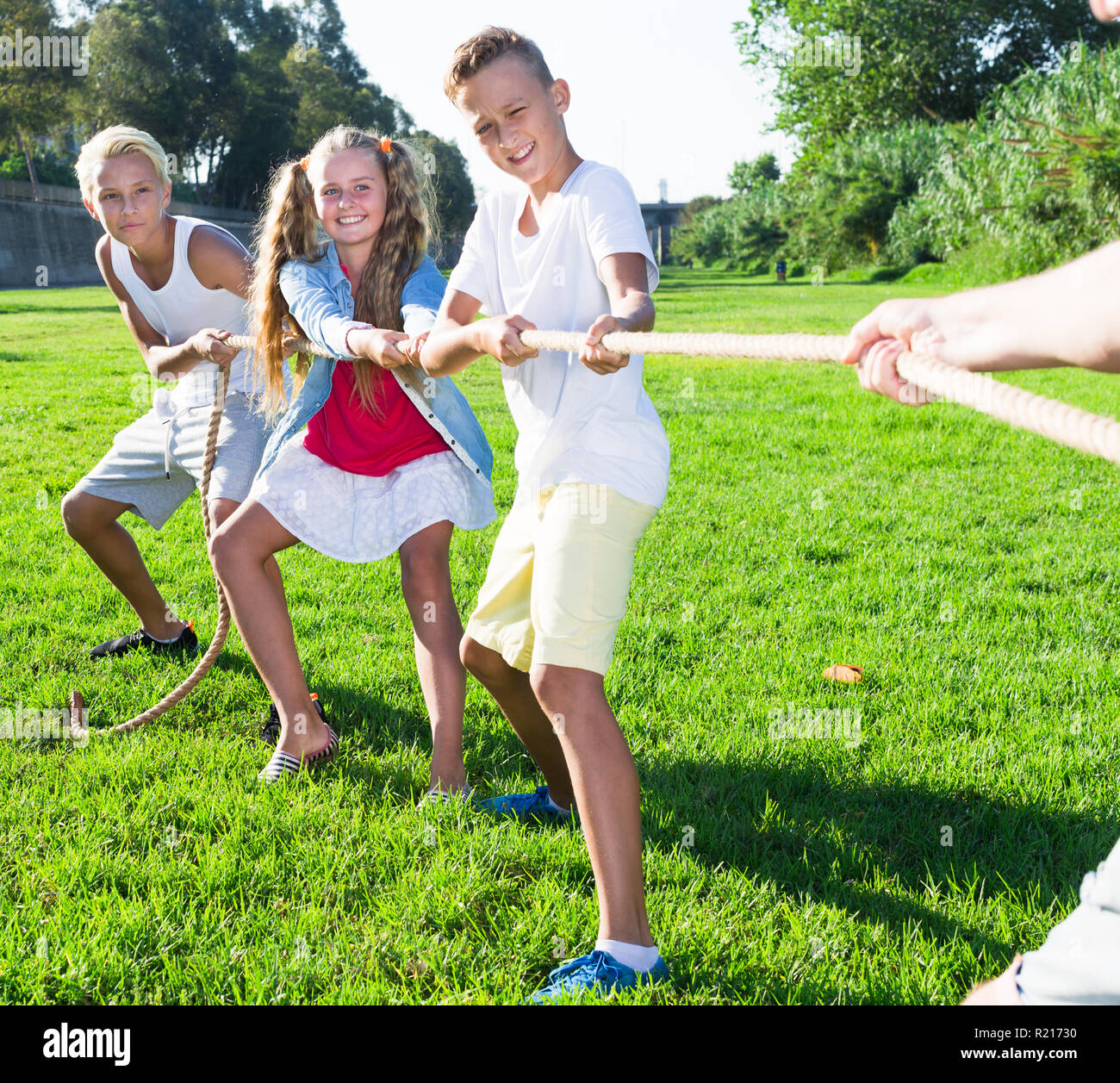 Group of laughing children having fun together outdoors pulling rope ...