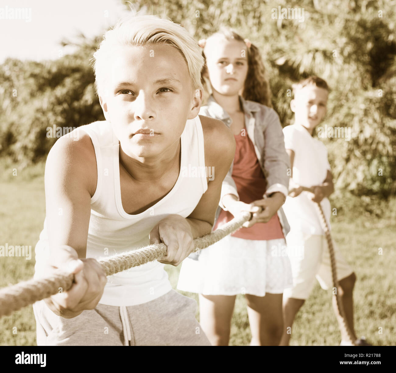 Group of laughing children having fun together outdoors pulling rope ...