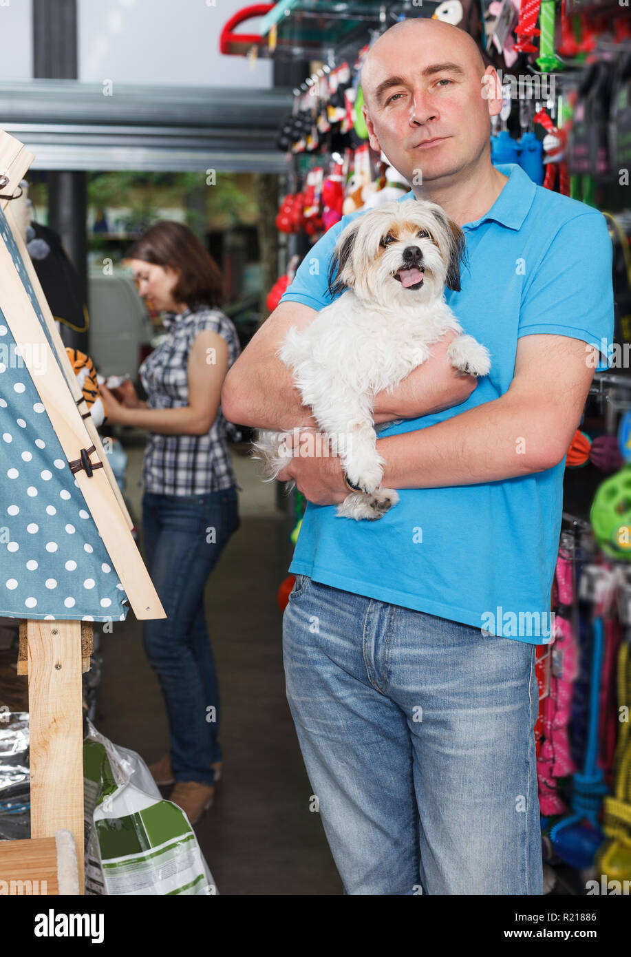 Attractive young male customer with dog looking new goods in pet store ...