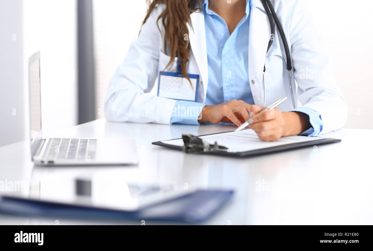 Unknown doctor woman filling up medical form while sitting at the desk ...