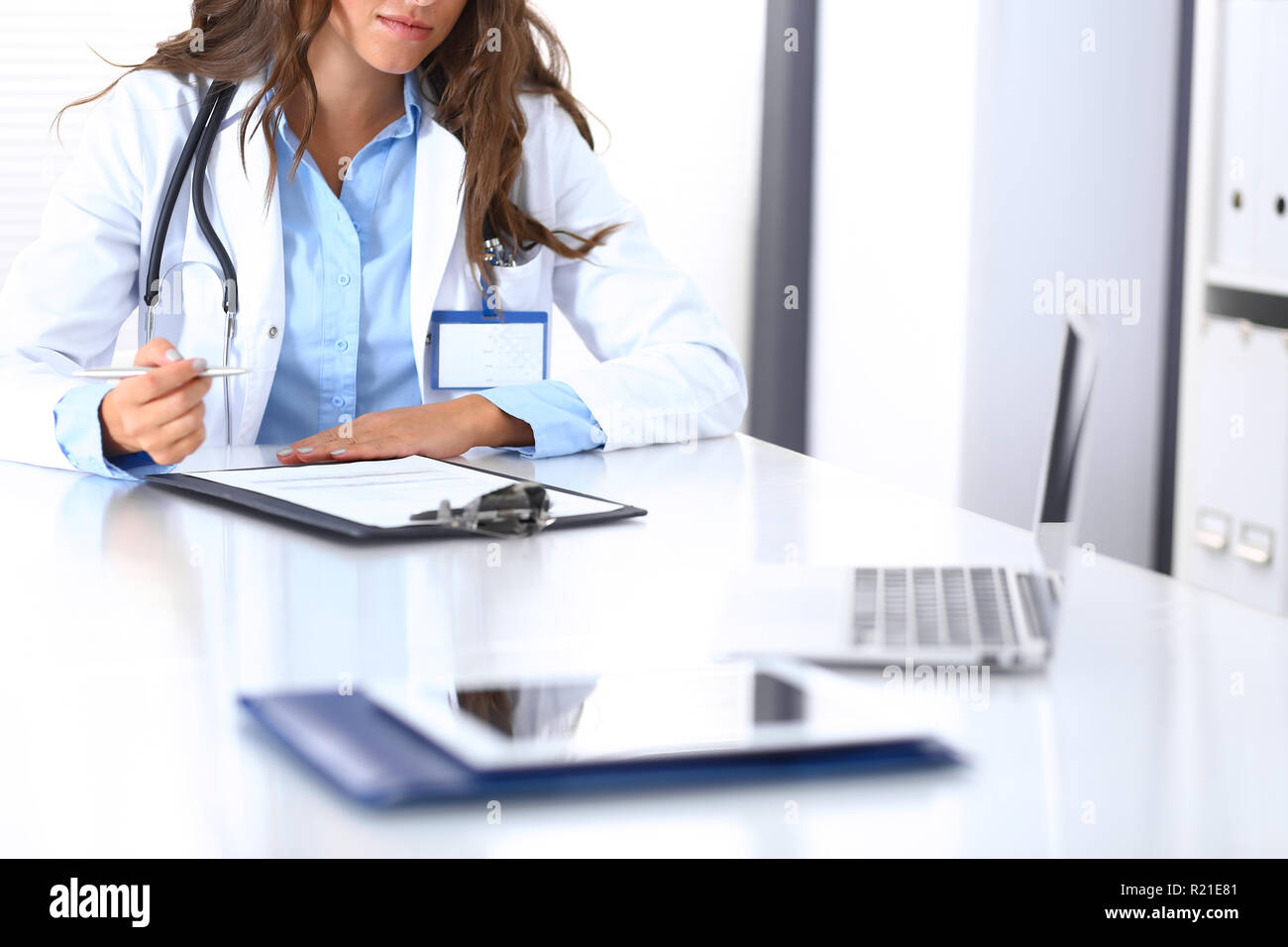 Unknown doctor woman filling up medical form while sitting at the desk ...