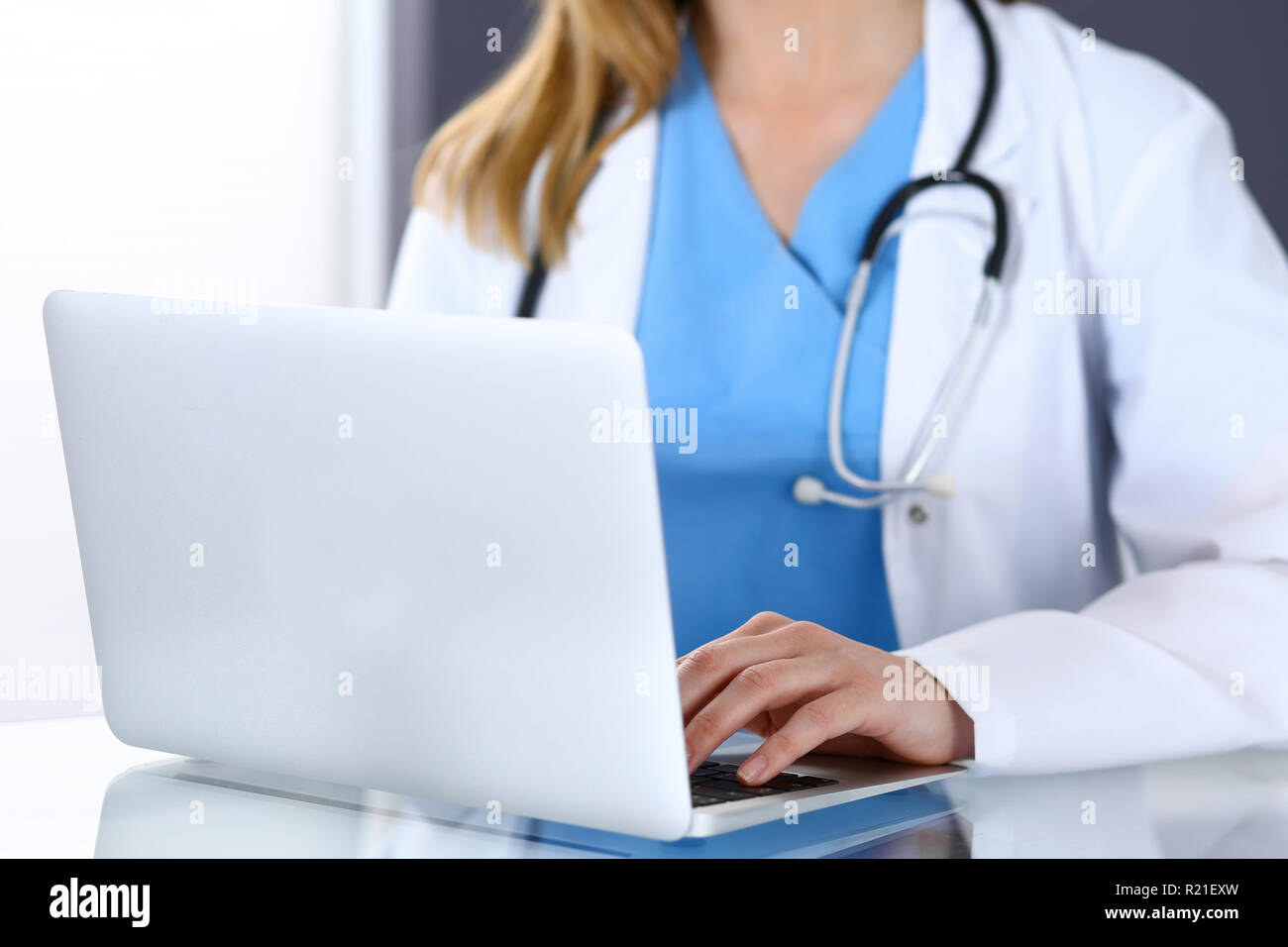 Doctor typing on laptop computer while sitting at the glass desk in ...