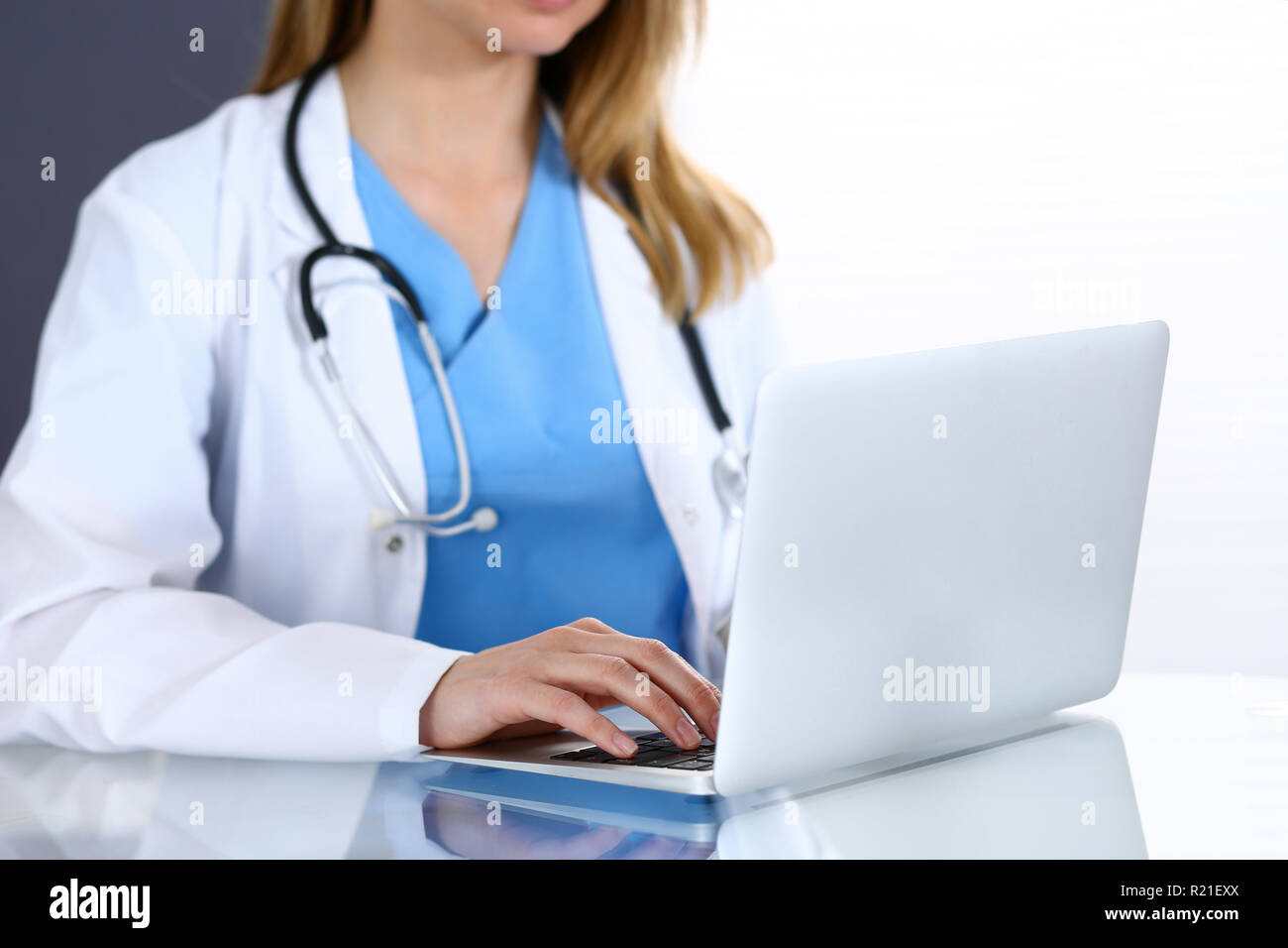 Doctor typing on laptop computer while sitting at the glass desk in ...