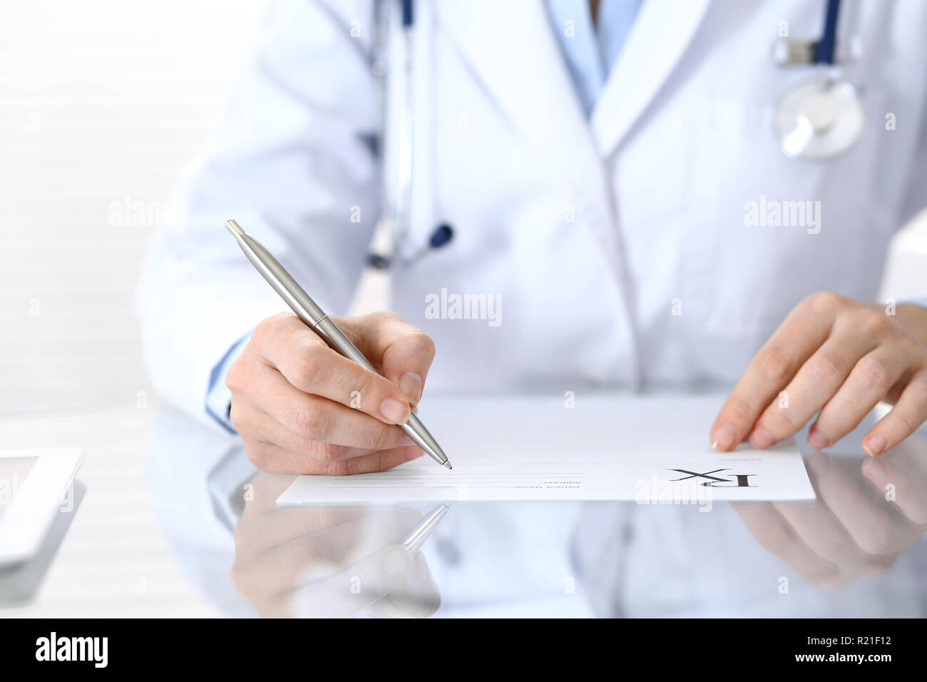 Doctor writing prescription form while sitting at glass desk in ...