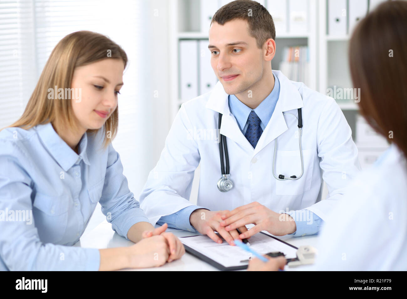 Two doctors and patient sitting at the table in medical cabinet Stock ...