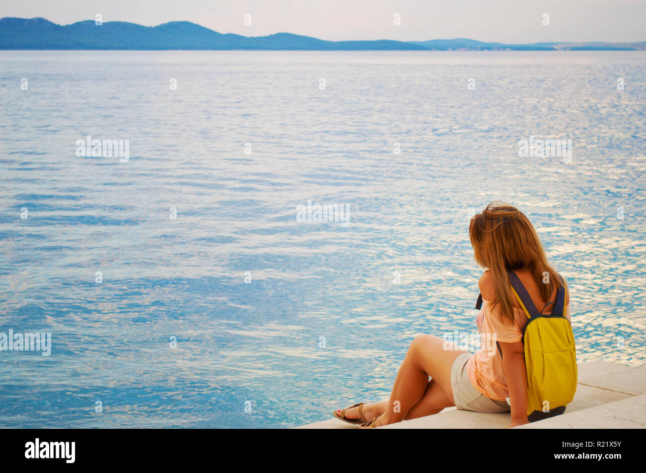 One young girl with a backpack sitting peacefully sideways on the stone ...