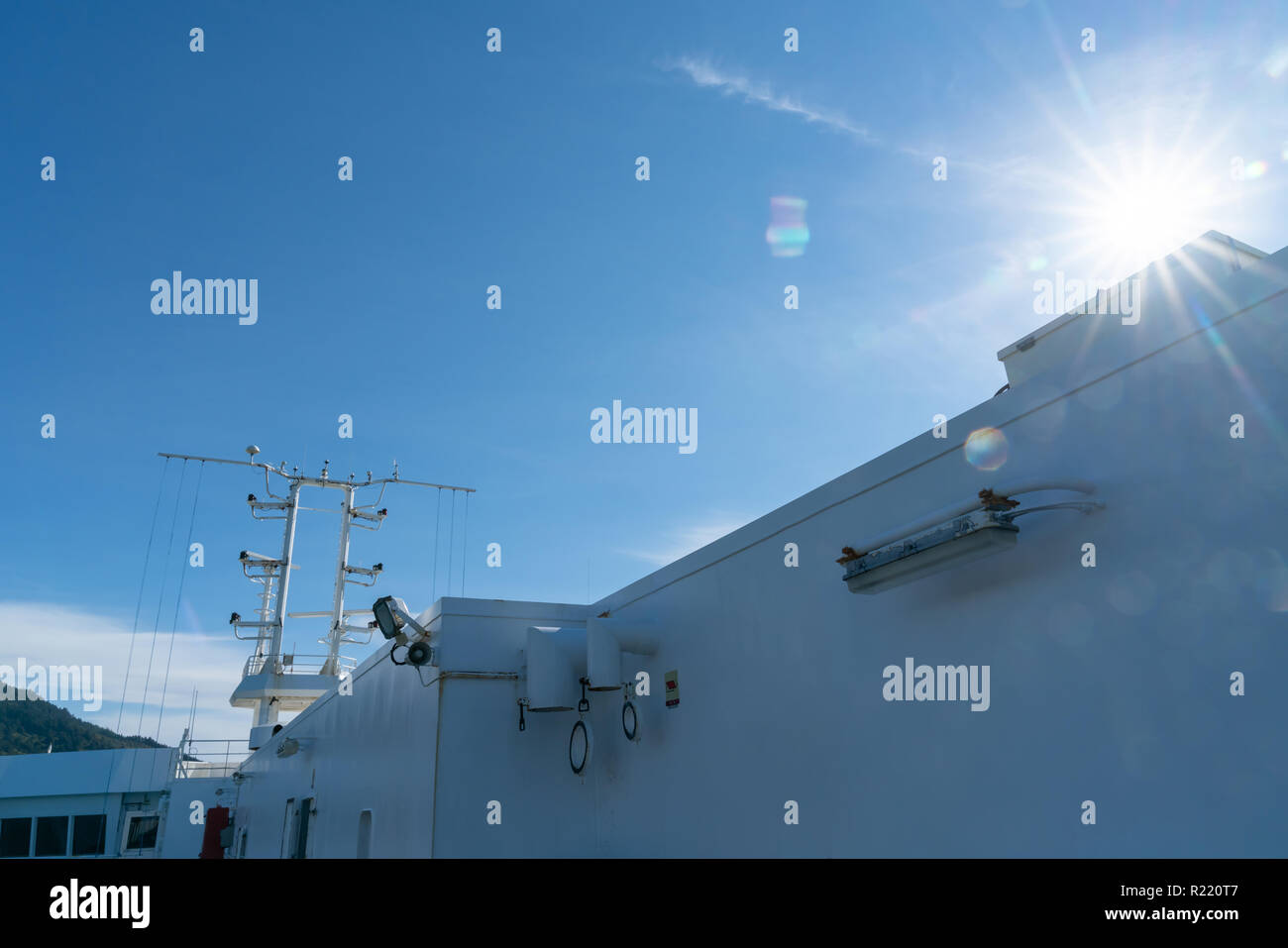 Lens flare from sun bursting over super-structure of ship against blue ...