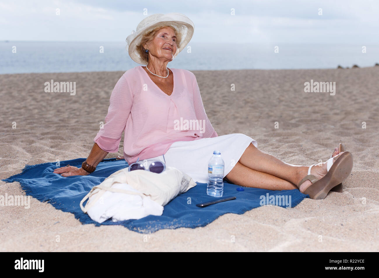 Happy retired woman sitting relaxed on sand at beach Stock Photo - Alamy