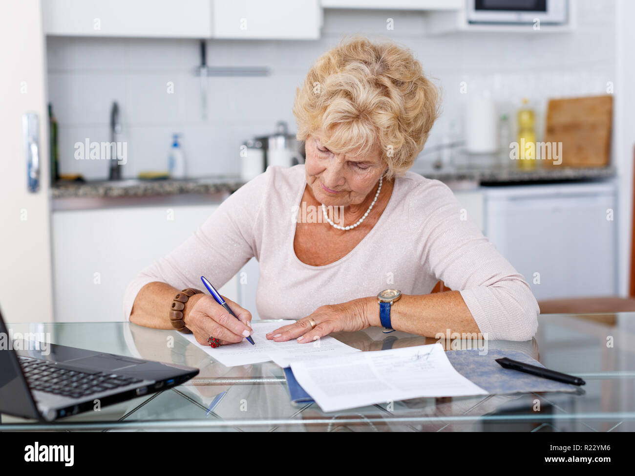 Attractive mature woman filling up documents at kitchen table Stock ...