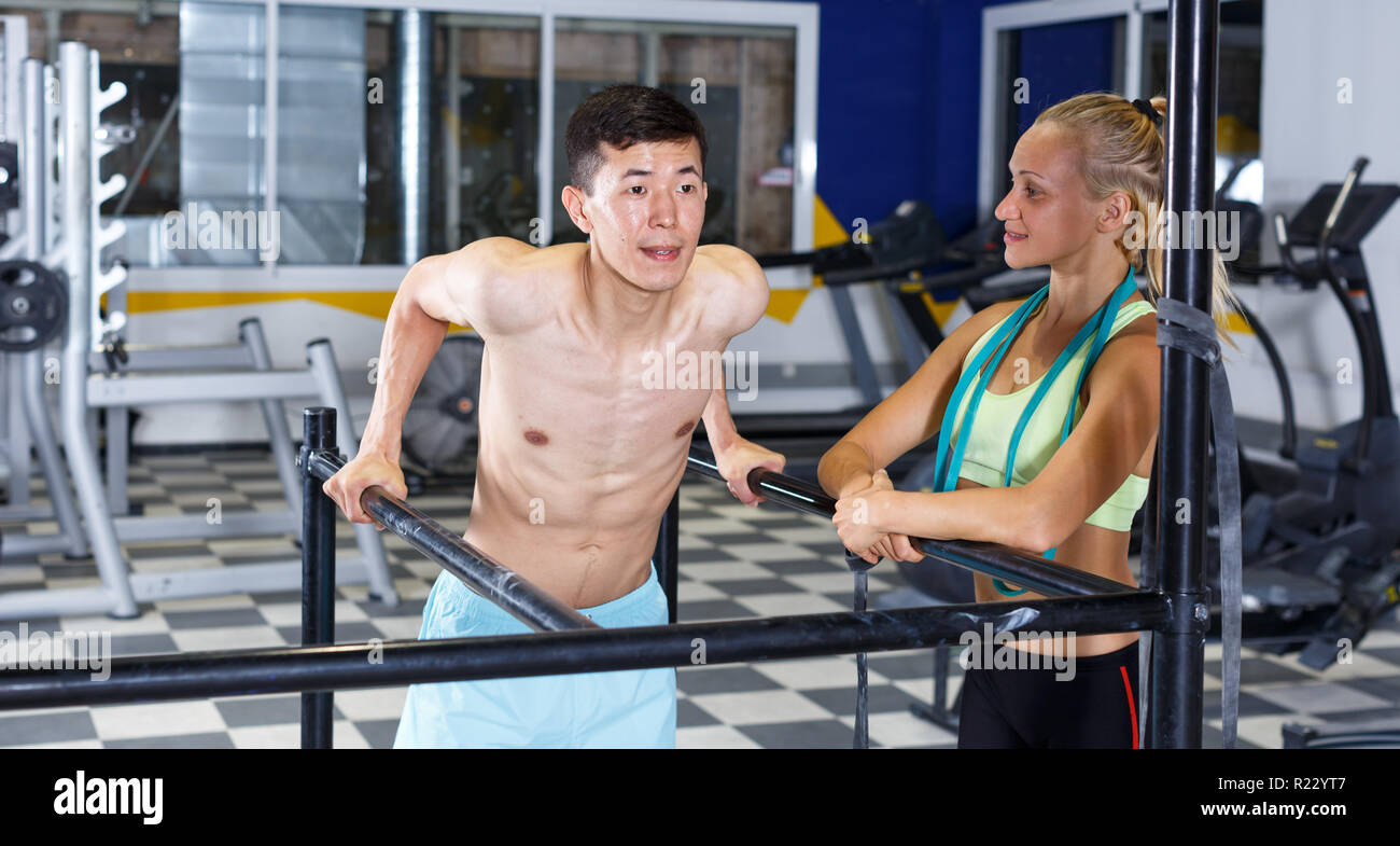 Male working out triceps and biceps on bars indoors with personal ...