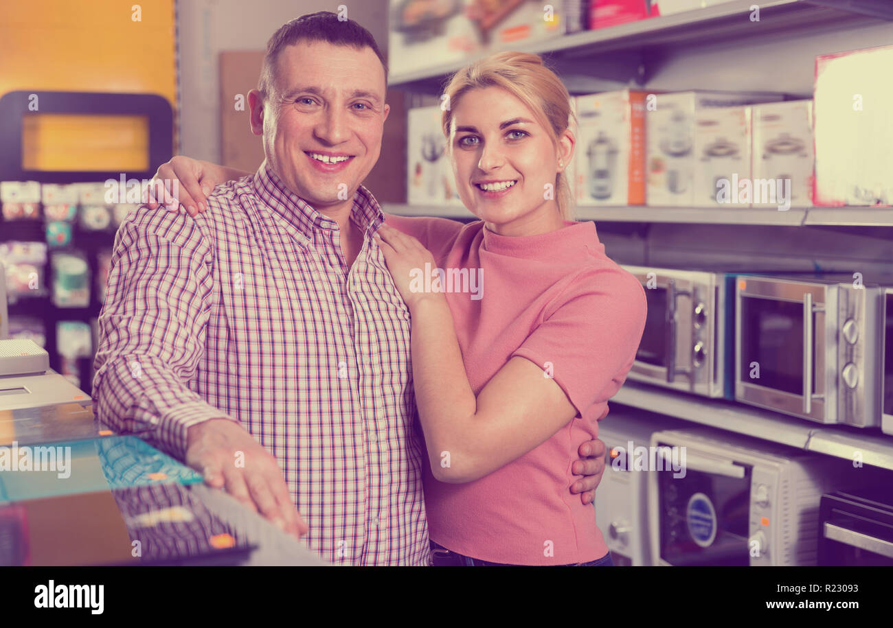 Positive glad cheerful couple standing in store of household appliances ...