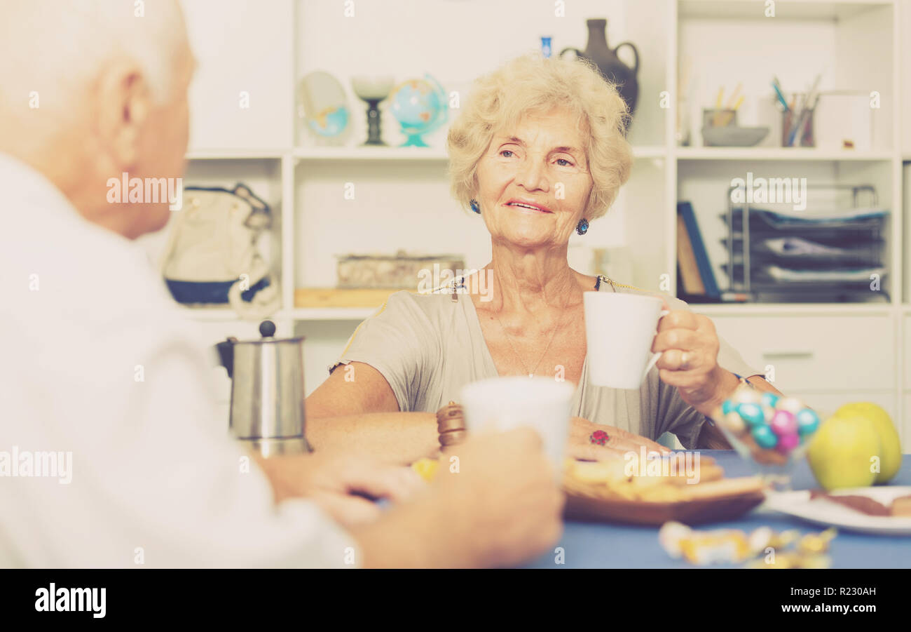 Smiling elderly woman enjoying time at home, drinking tea with husband ...