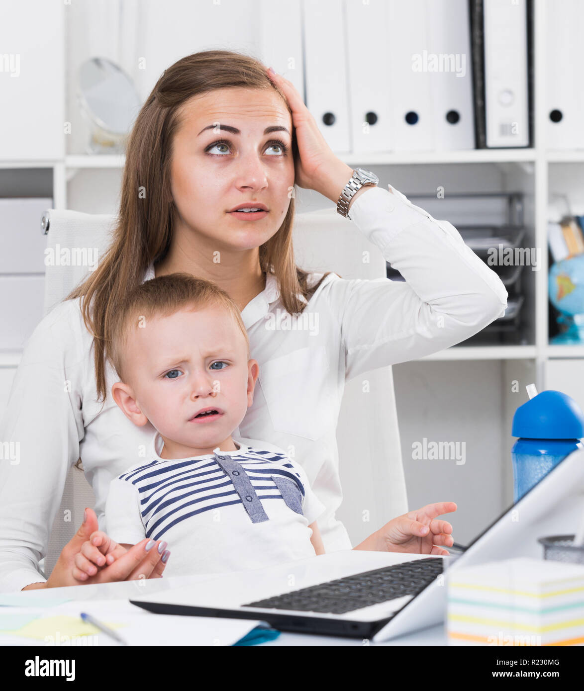 Perplexed mom with kid is having issue while working behind laptop in ...