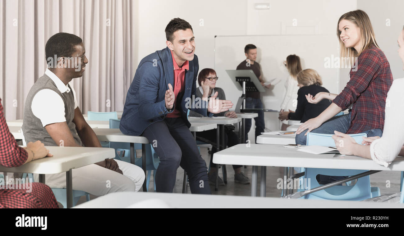 Happy group of adult students lively chatting while enjoying free time ...