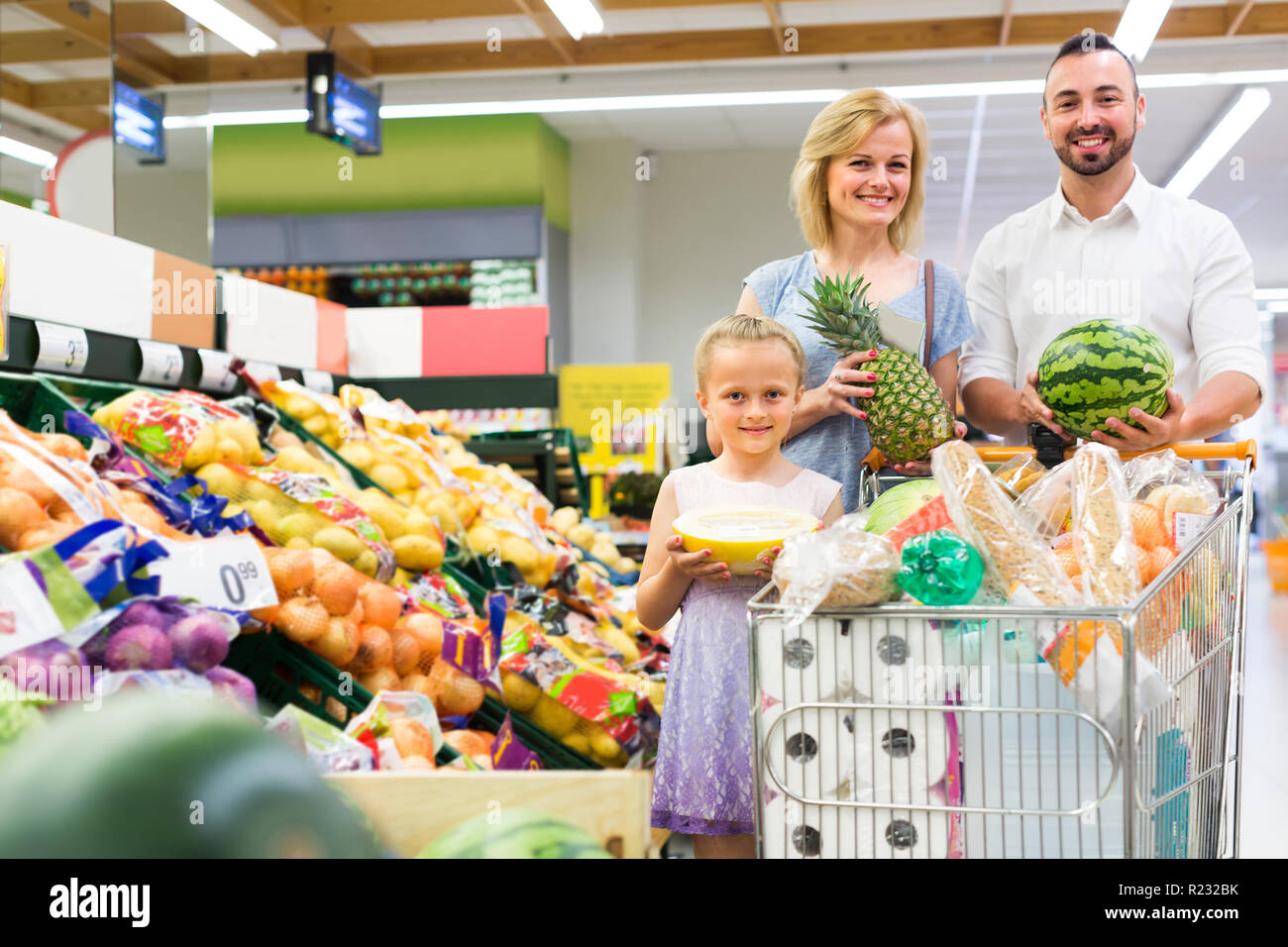 Cheerful smiling parents with little daughter in fruit section in ...