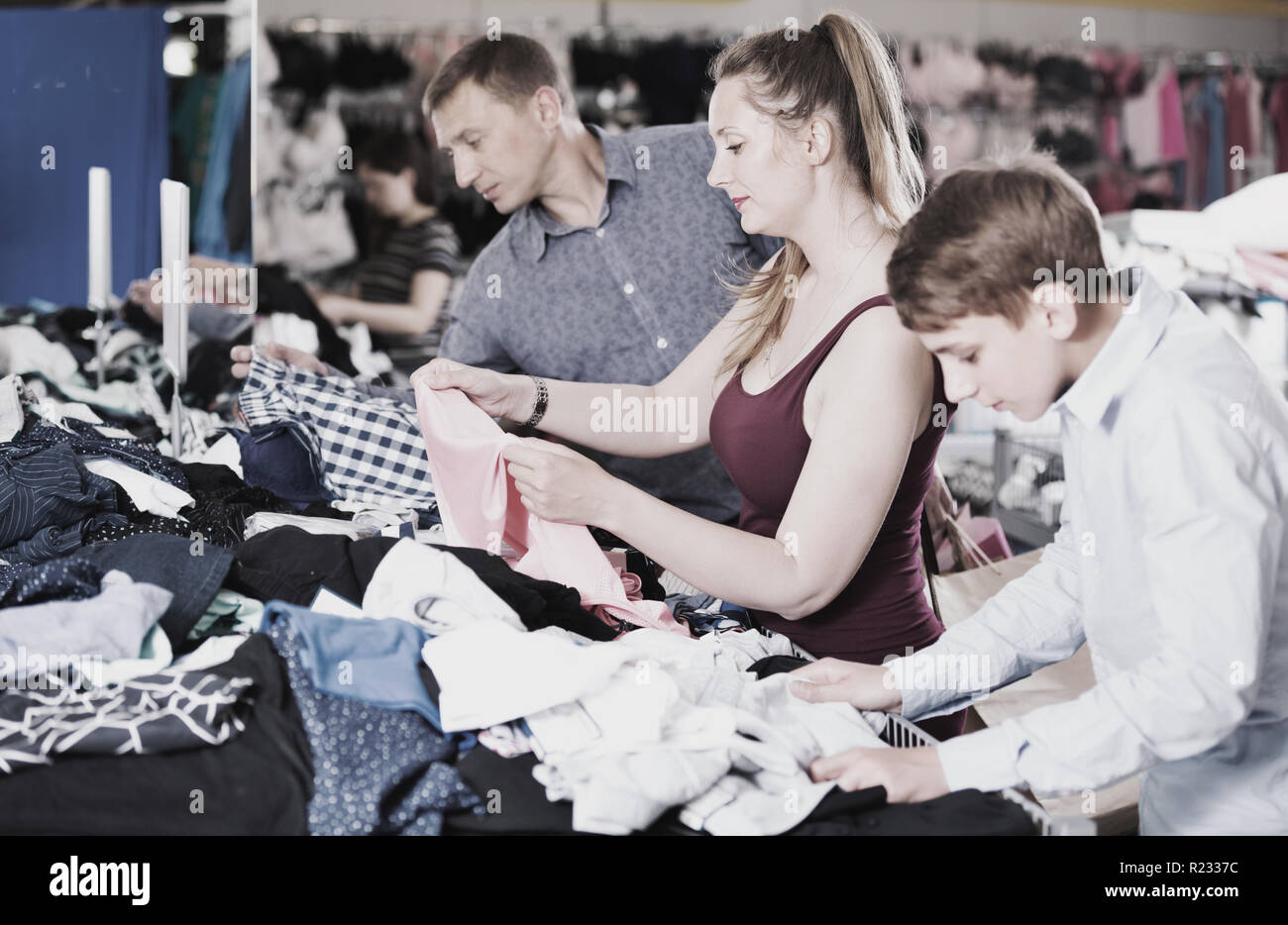 Positive family of three with teenager choosing clothes a half-off sale ...