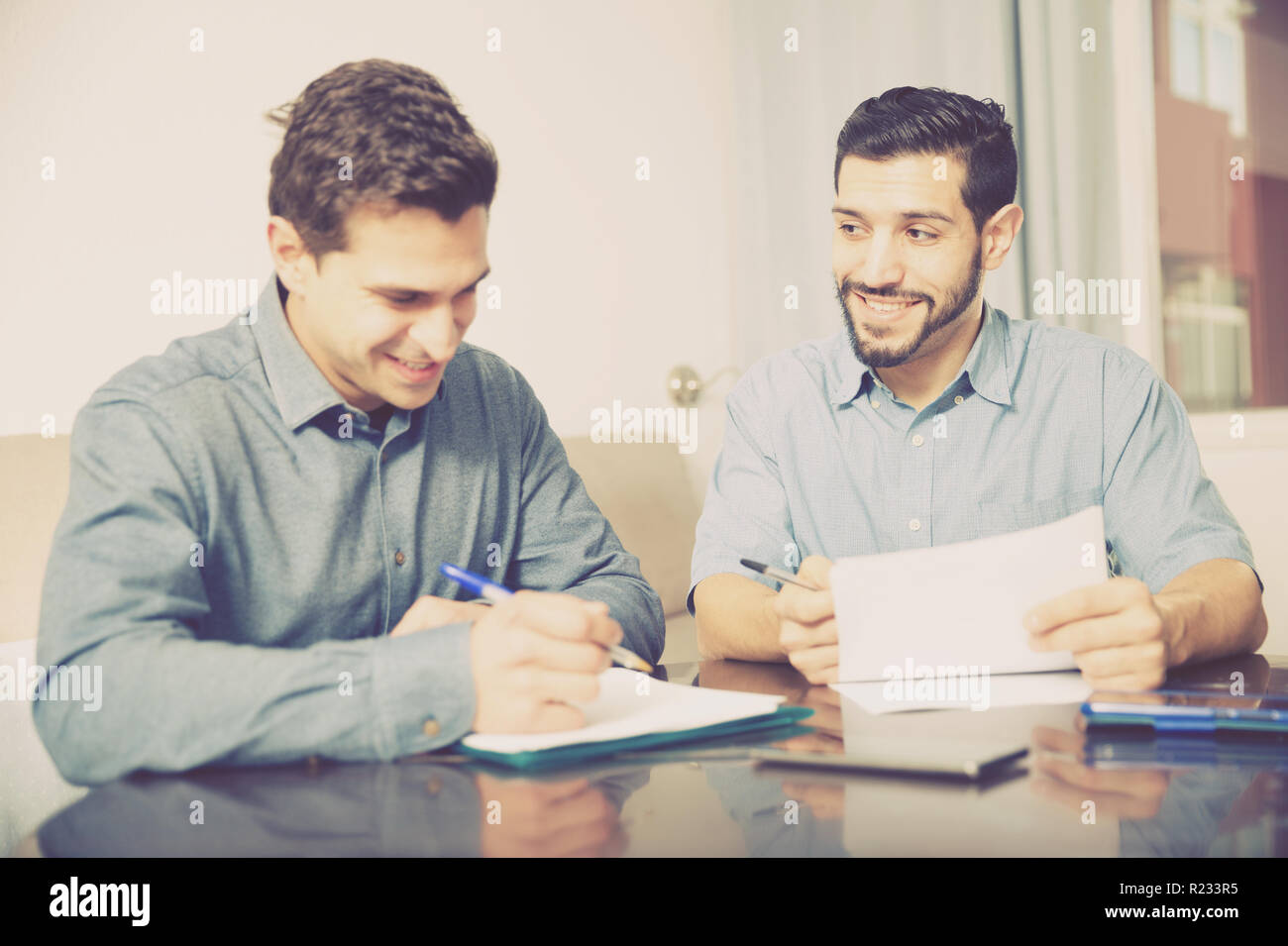 Portrait of two cheerful young men reading documents together at home ...