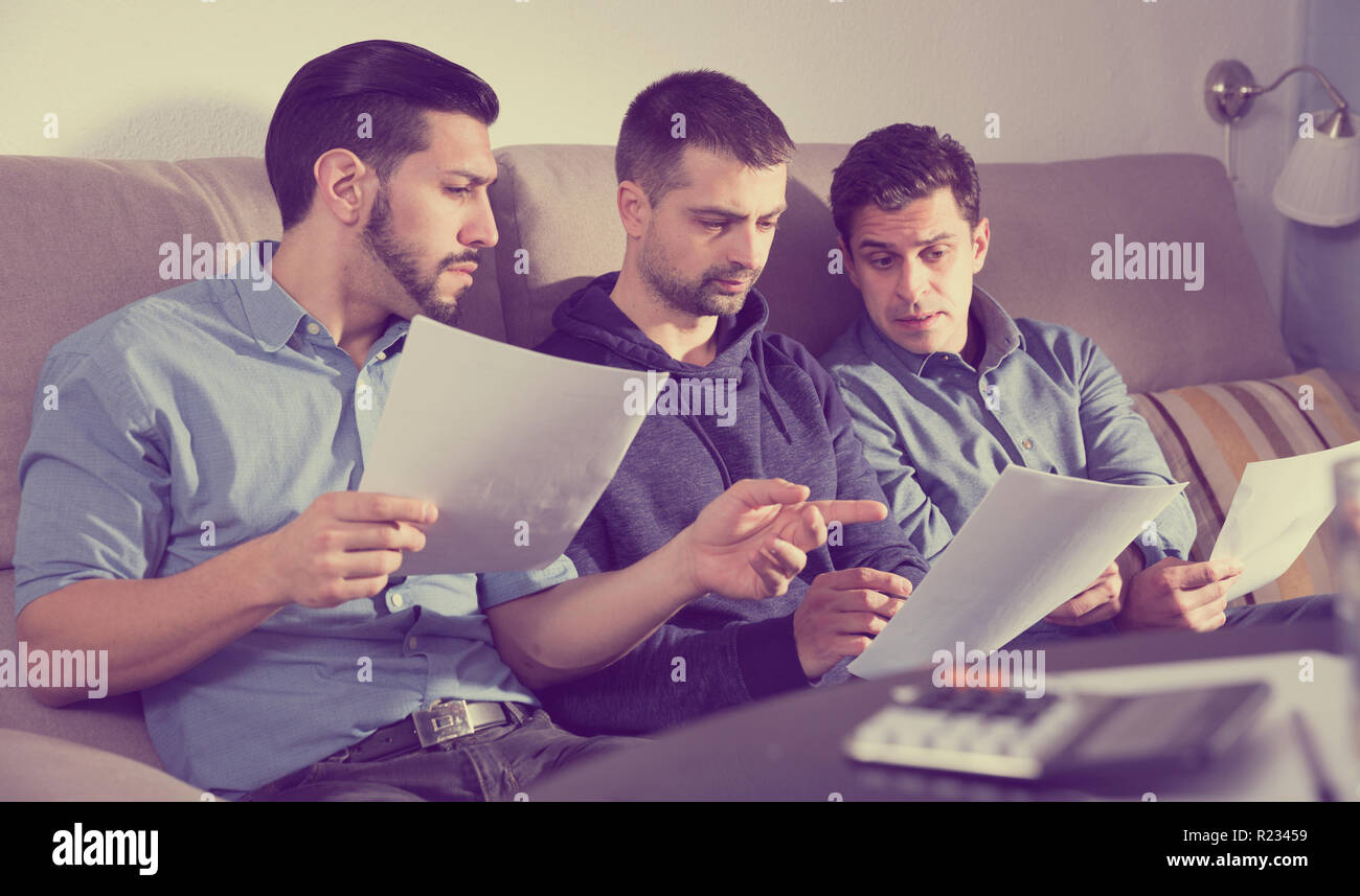 Three young men in serious discussion while analysing documents ...