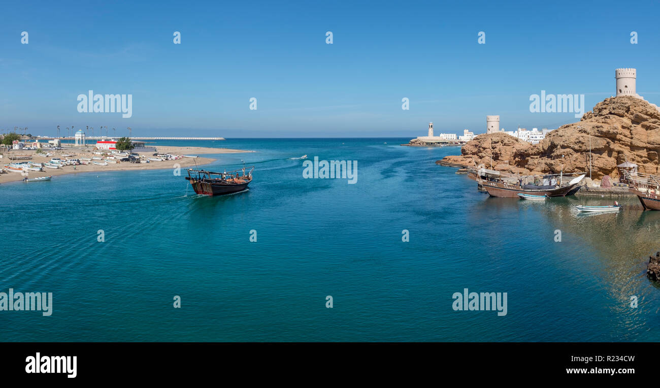 Fishing boat sailing out of the harbour past a watchtower at Sur, Oman ...