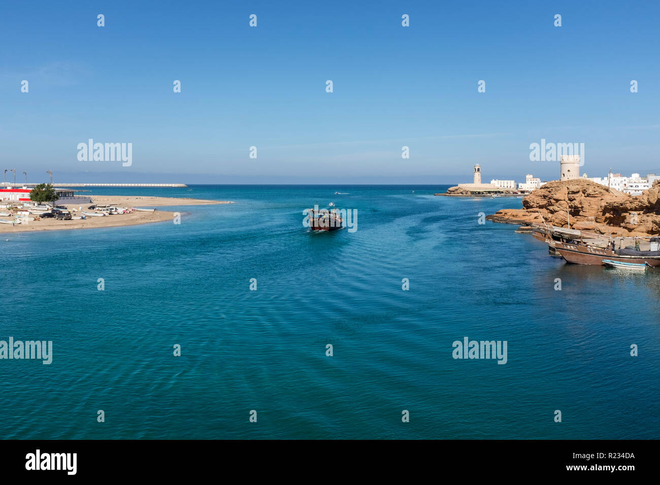 Fishing boat sailing out of the harbour past a watchtower at Sur, Oman ...