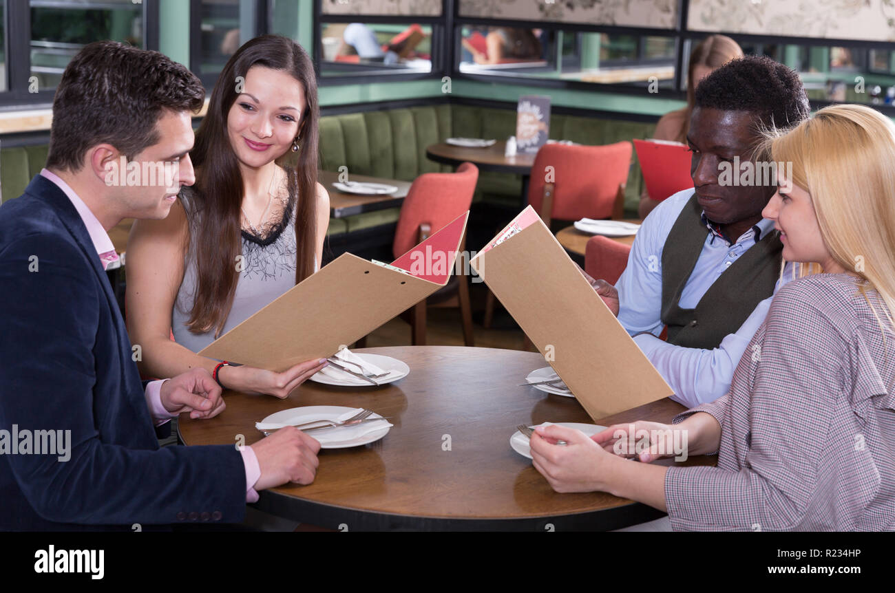 Сheerful friends choosing dishes from menu card in restaurant Stock ...