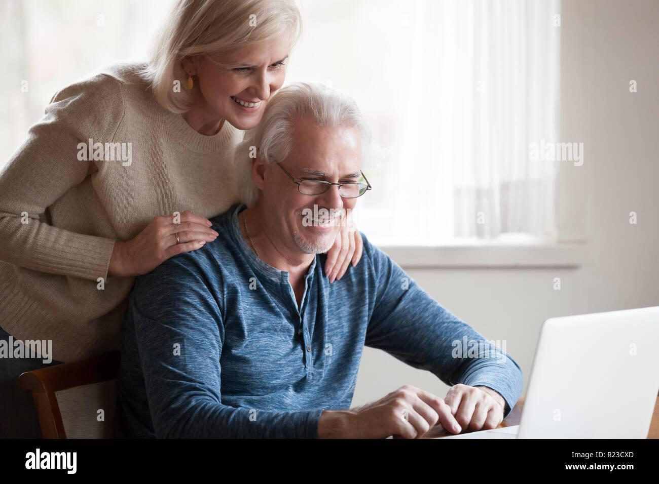 Excited aged husband using laptop showing smiling wife something on ...