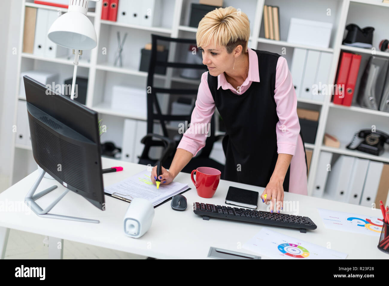 A young girl stands near the Desk in the office and typing on the ...