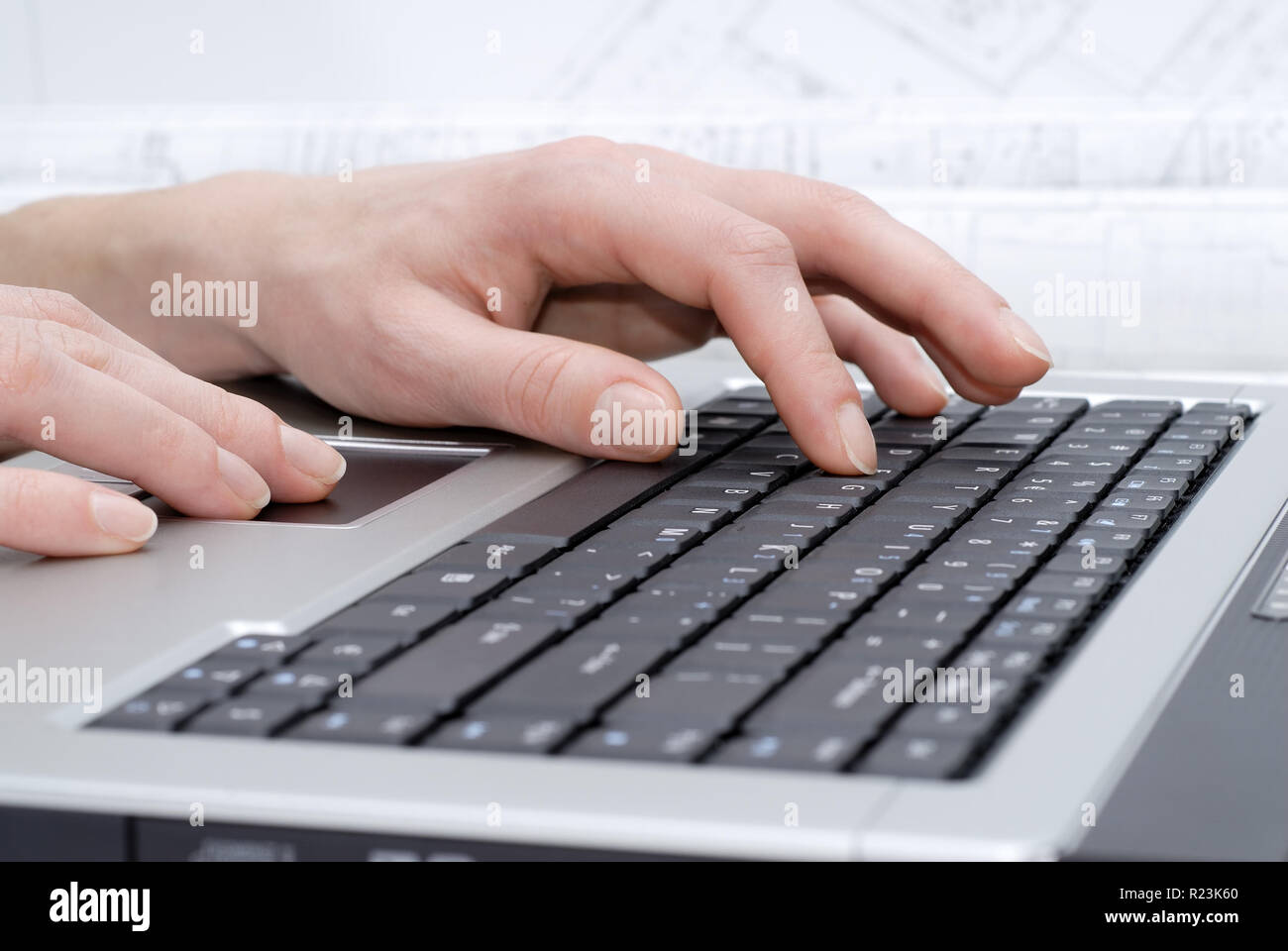 Female hands on laptop keyboard. Architectural plans in background ...