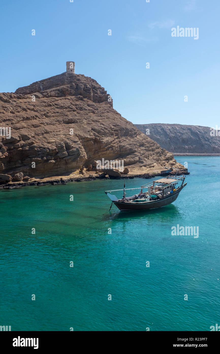 A watchtower and a wooden dhow boat in Sur, Oman. Sur is known for its ...