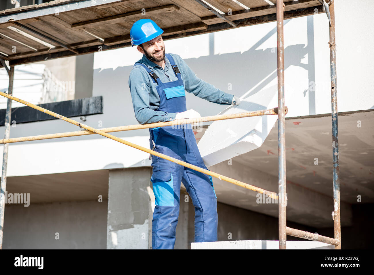 Funny portrait of a builder warming a building facade with foam panels ...