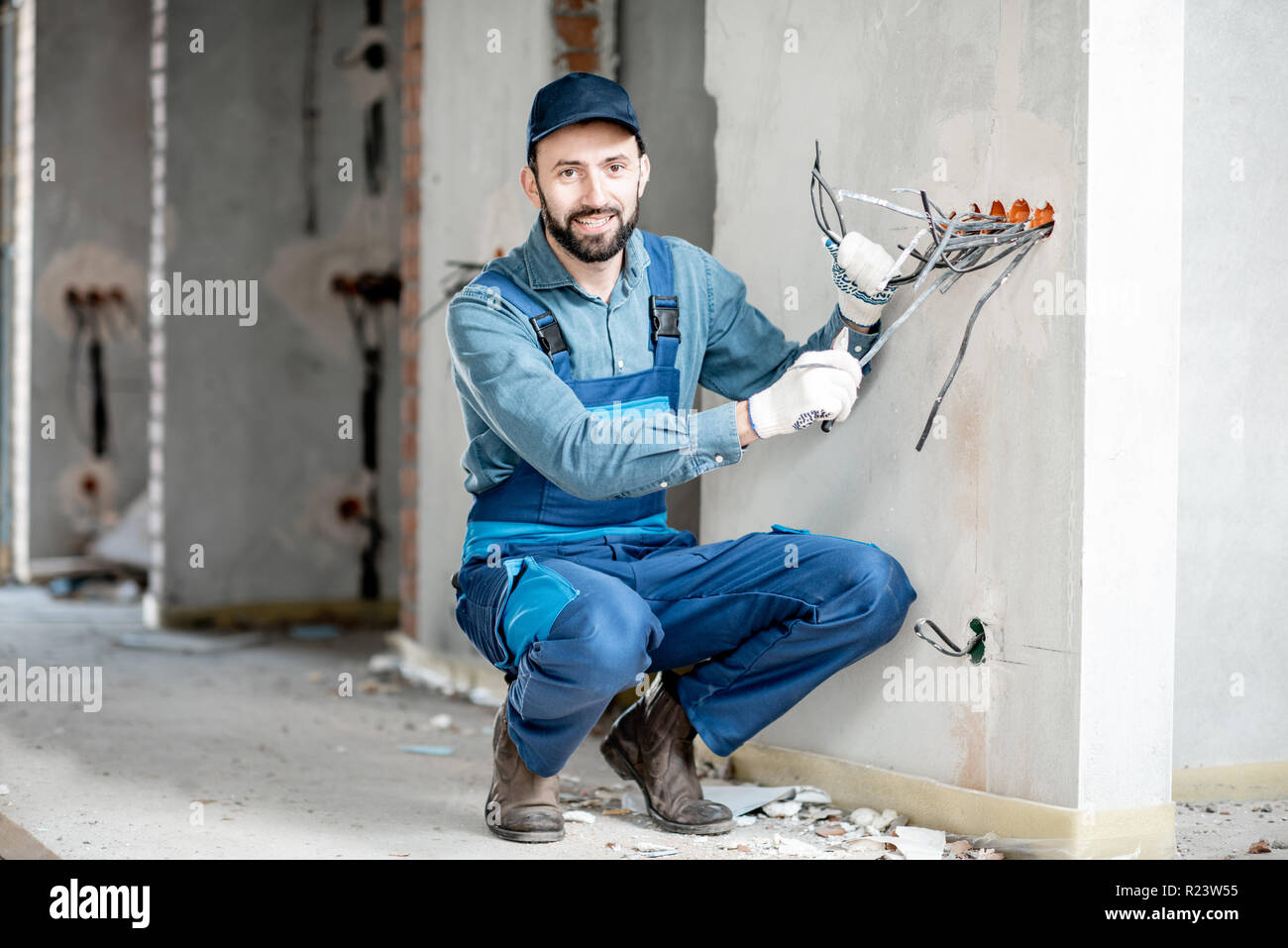 Portrait of an electrician mounting wiring for electric sockets on the ...