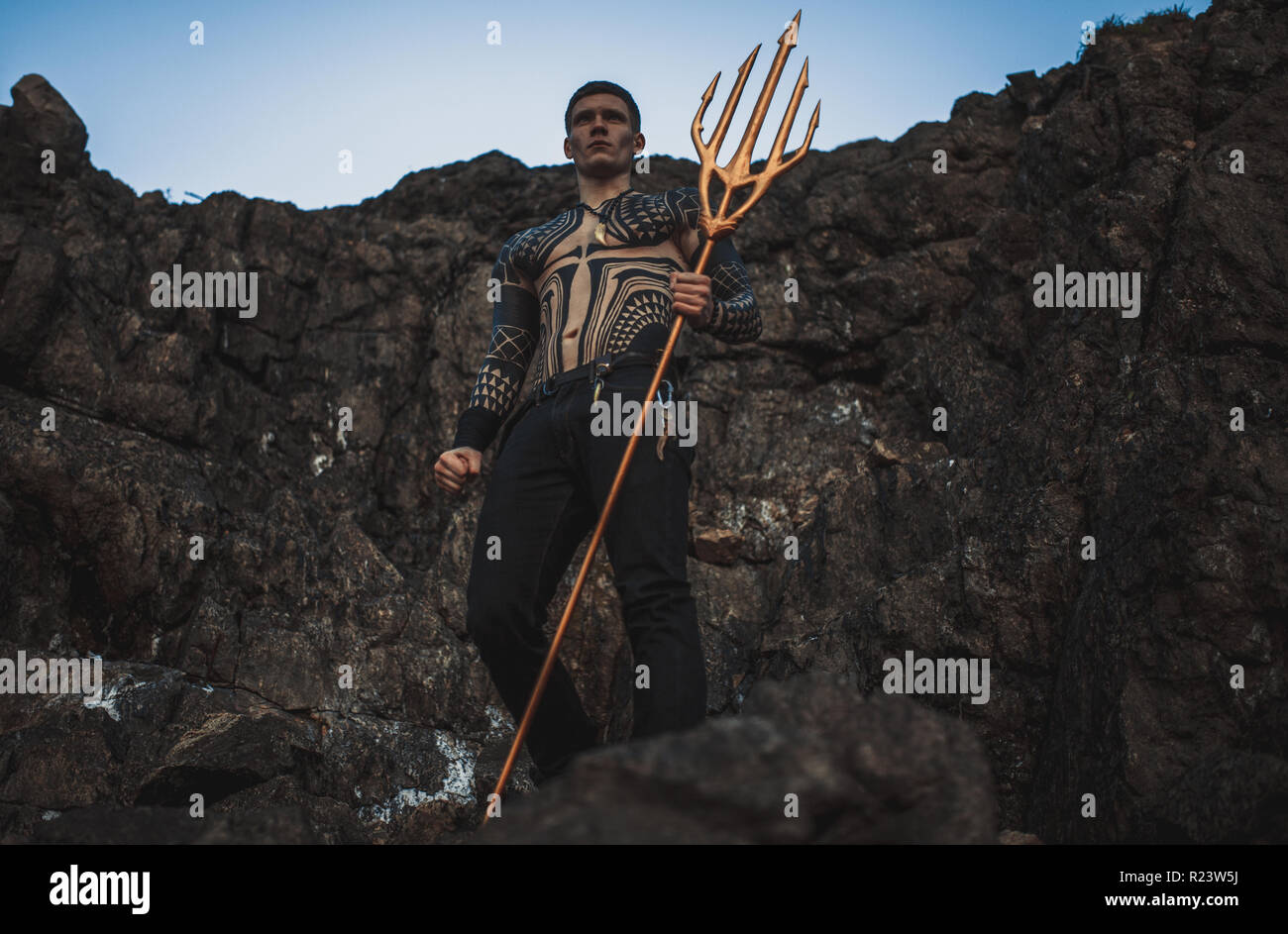 A young man in armor with a trident in his hands against the background ...