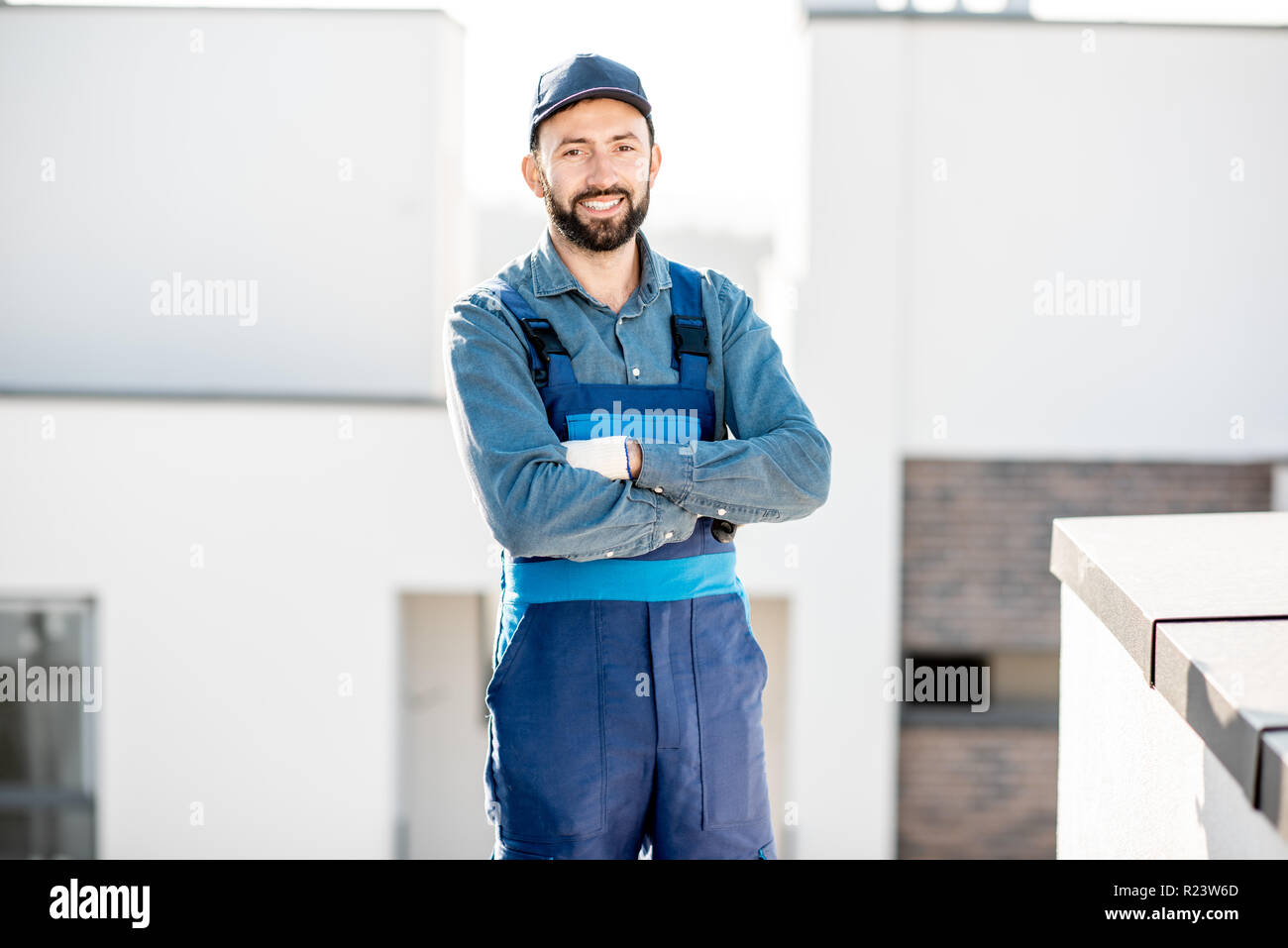 Portrait of a builder in uniform on the roof of a new white building ...