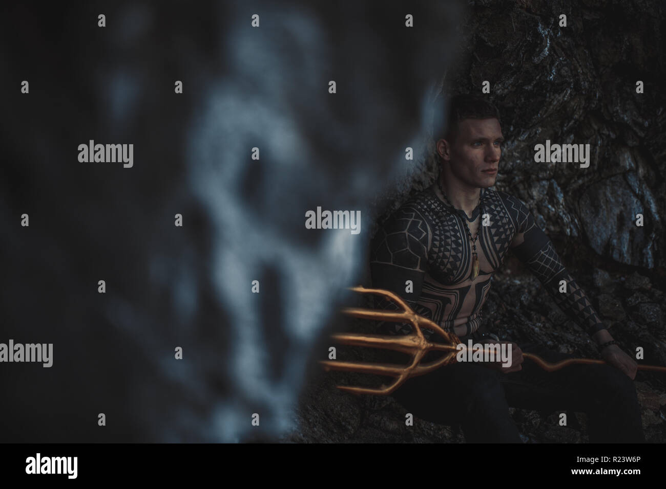 A young man in armor with a trident in his hands against the background ...