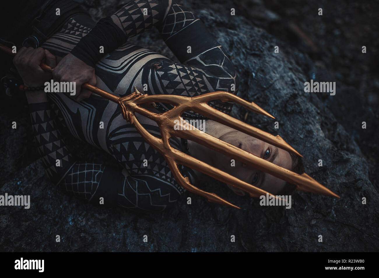 A young man in armor and with a trident in his hands lies on the rock ...