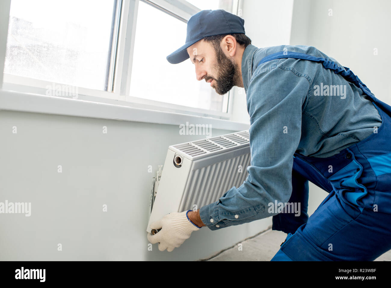 Workman mounting water heating radiator near the window in the white ...