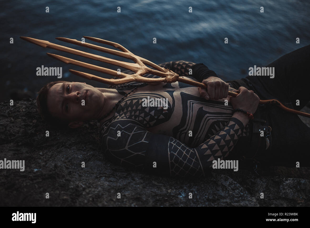 A young man in armor and with a trident in his hands lies on the rock ...