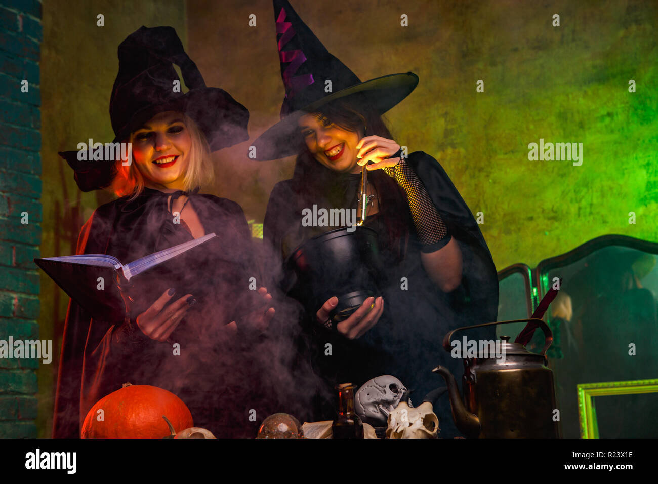 Portrait of smiling two witches in black hats reading book at table ...