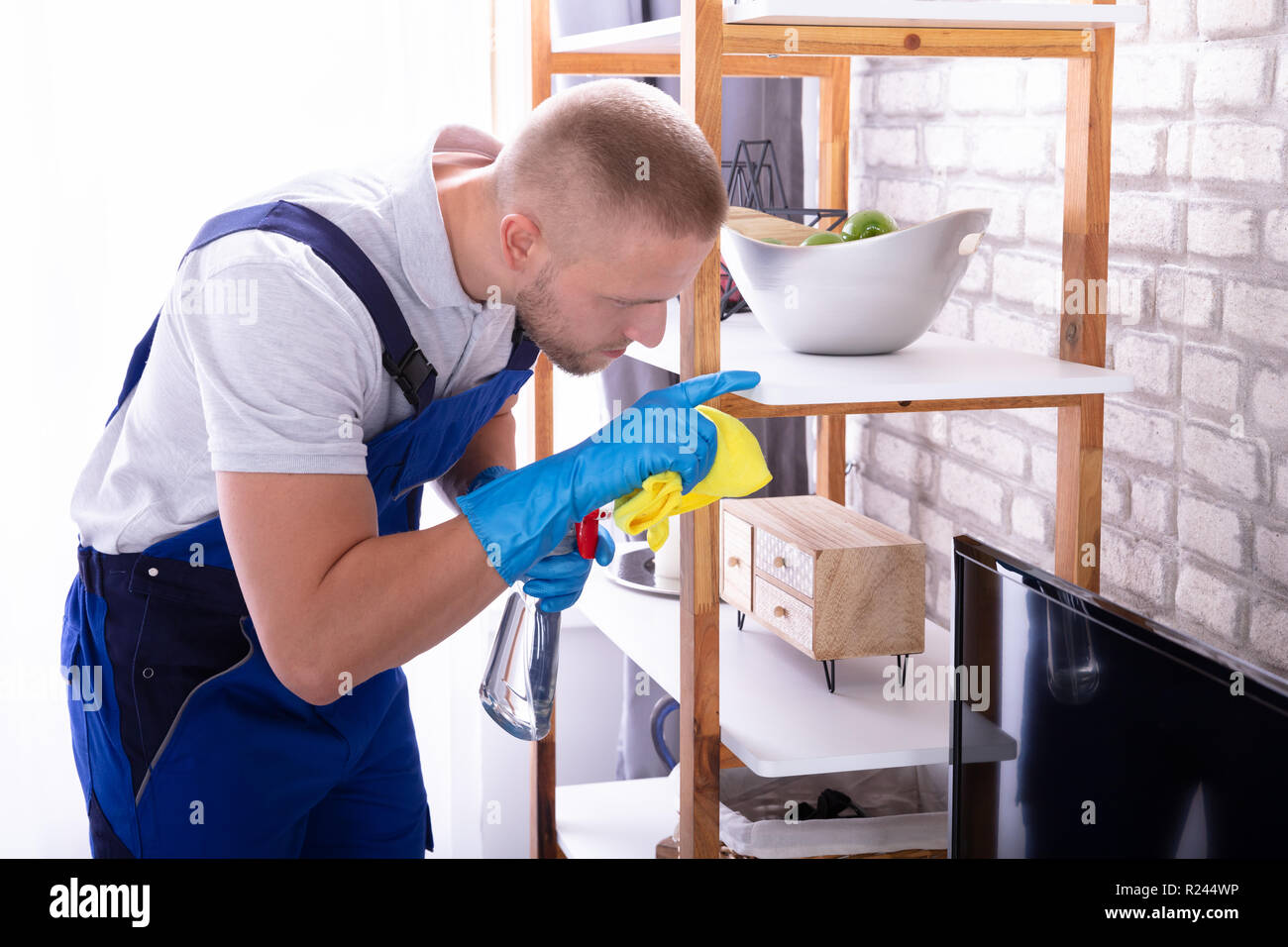 Side View Of A Young Male Janitor Cleaning Shelf In House Stock Photo ...
