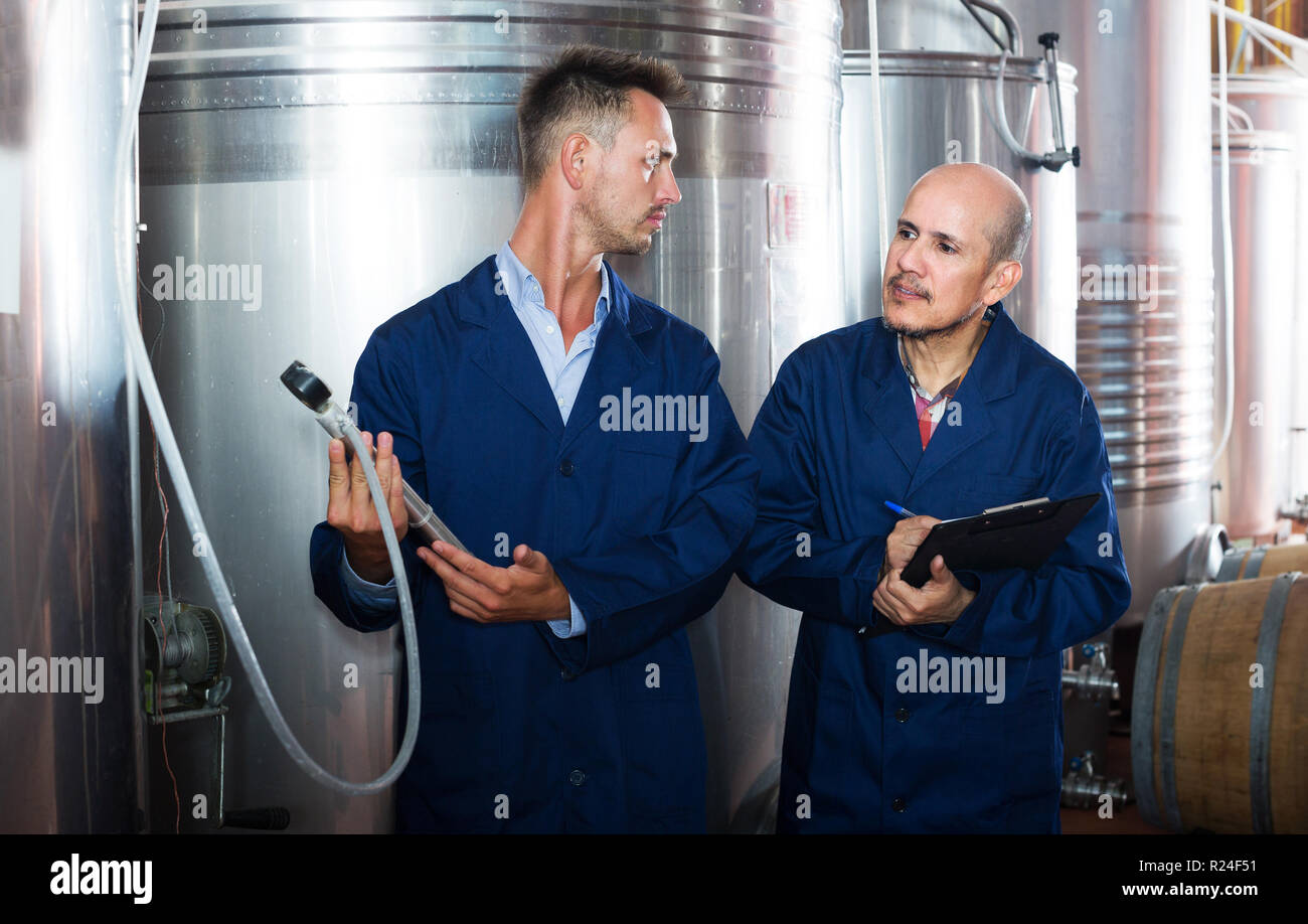 Adult serious winery workers taking notes while checking equipment in ...