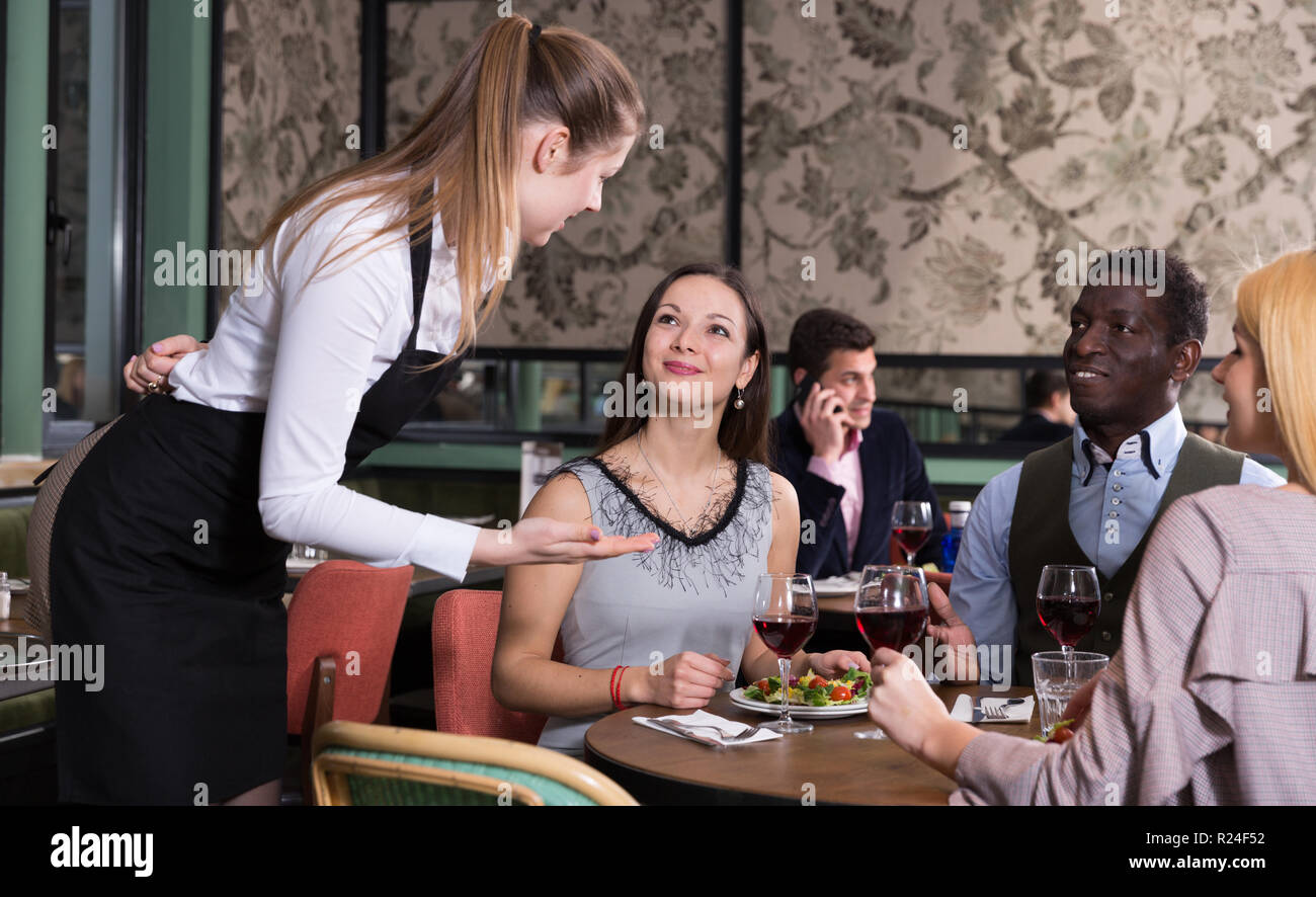 Positive elegant company of three sitting at restaurant table, talking ...
