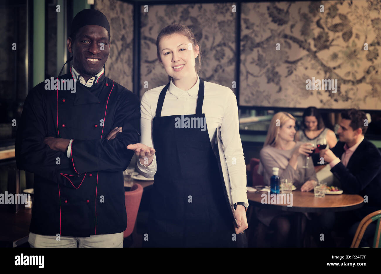 Polite happy positive smiling waitress standing in restaurant hall with ...