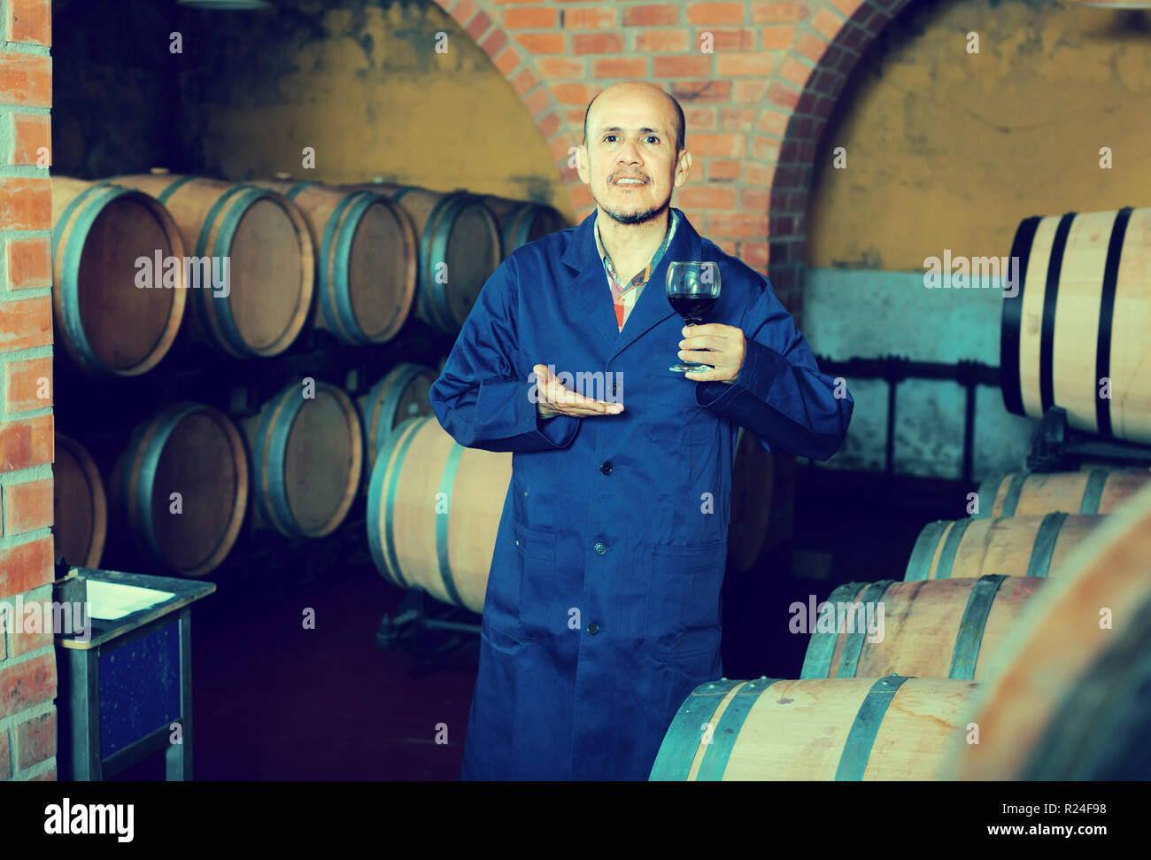 Mature winery worker wearing coat holding glass of wine in cellar Stock ...