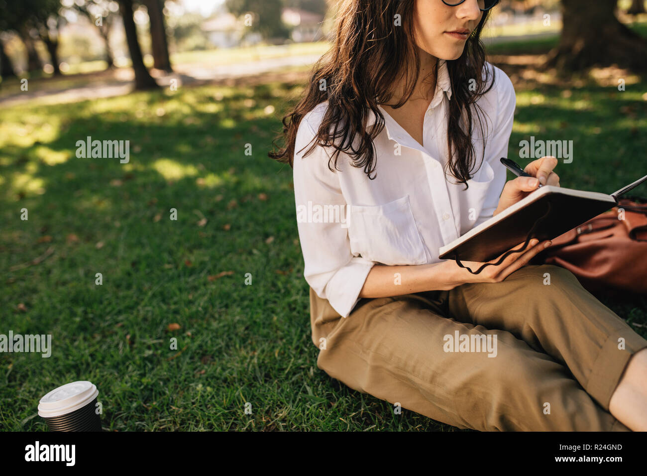 Woman sitting on grass at park with book making notes. Female relaxing ...