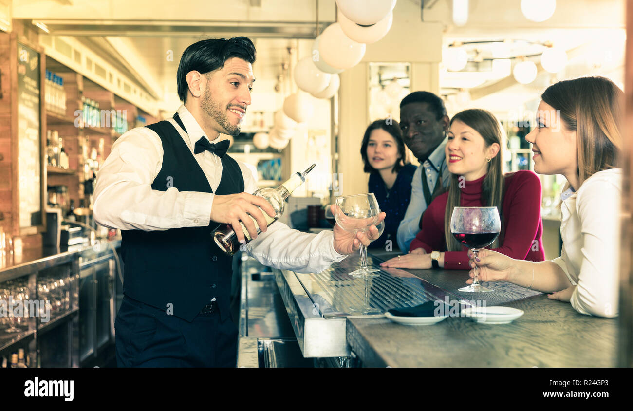Handsome hispanic barman serving drinks to young people on bar in ...