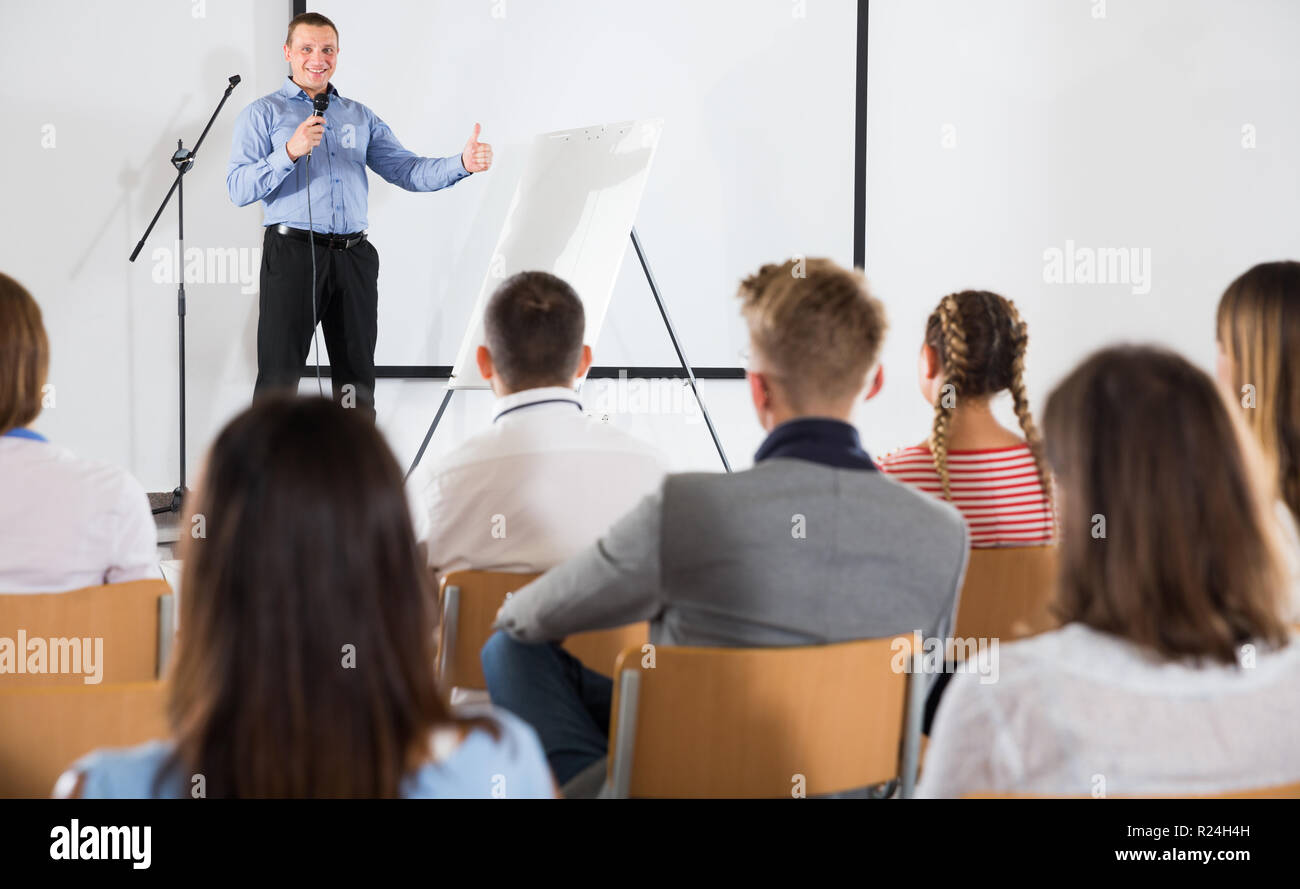 Positive male professor standing with microphone in auditorium ...