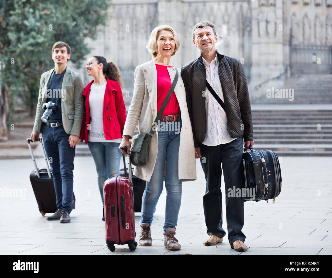 Two happy positive smiling couples with baggage sightseeing and smiling ...