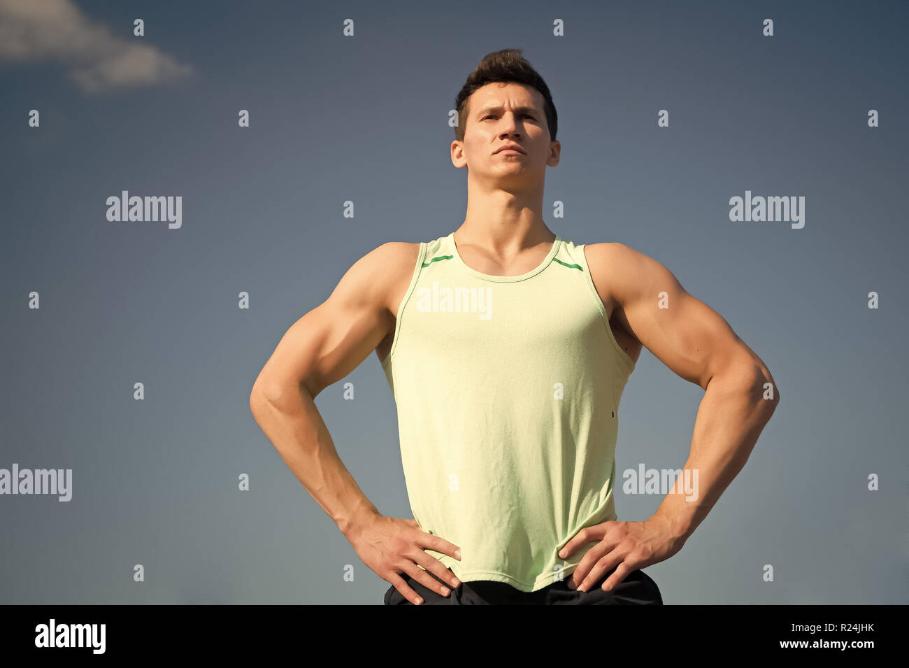 Athlete in green tshirt on sunny day. Man bodybuilder posing on blue ...