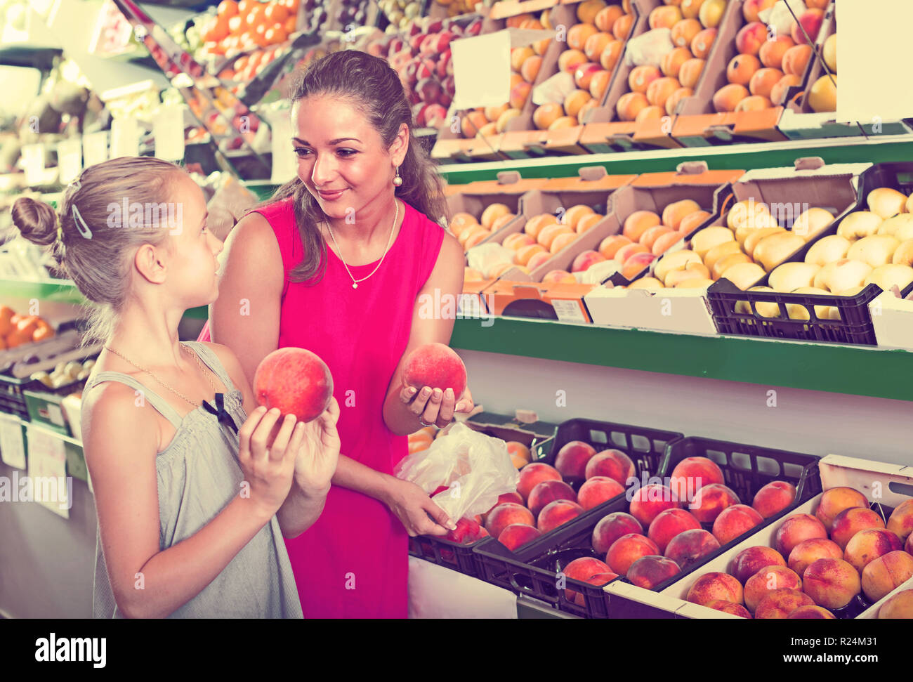 portrait of smiling mother with girl taking peaches on fruit market ...
