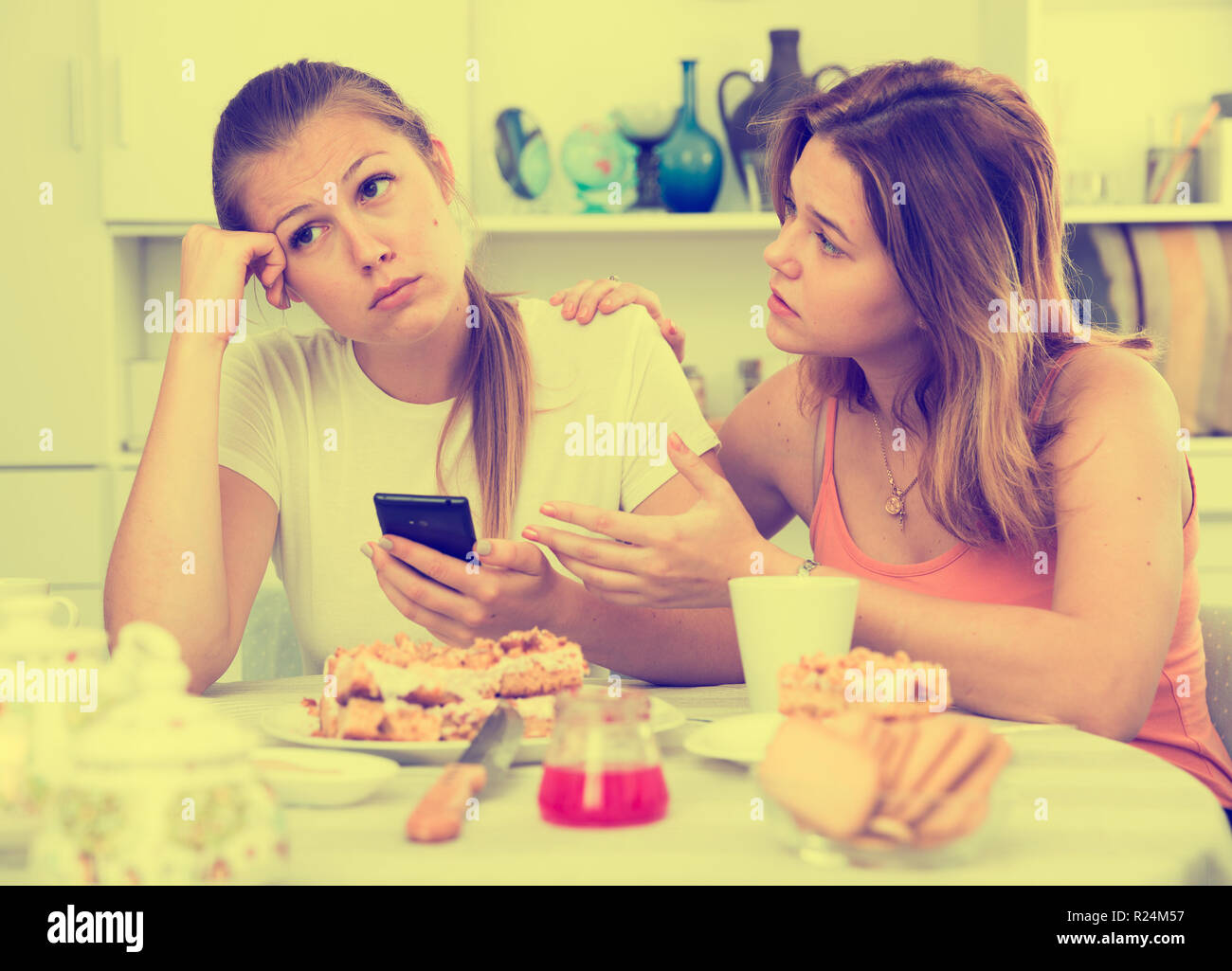 Portrait of female talking with sad girl friend with mobile at the ...